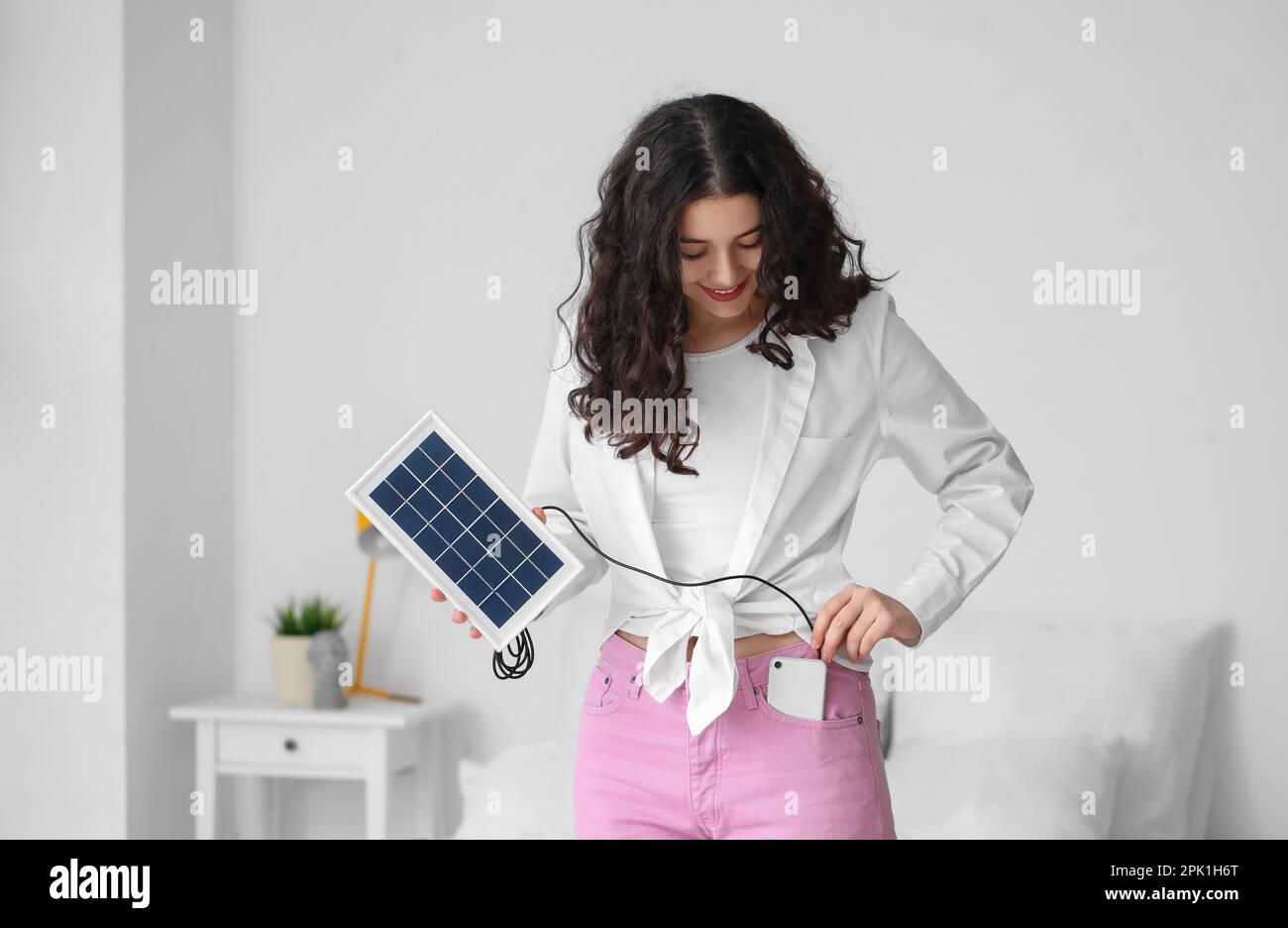 Teenage girl charging mobile phone with portable solar panel in bedroom ...
