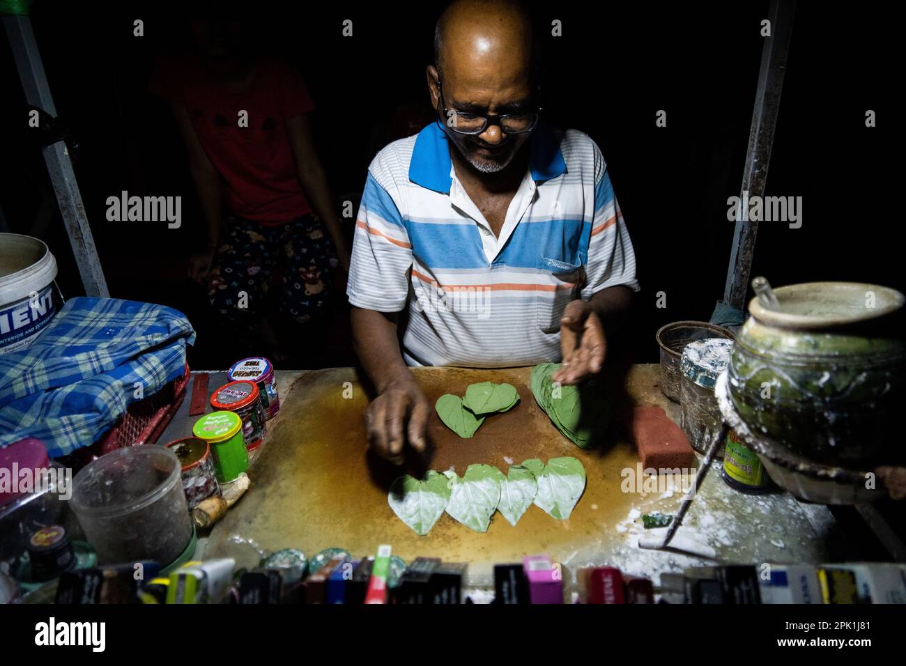 A betel nut vendor prepares their product under a tiny lamp powered by ...