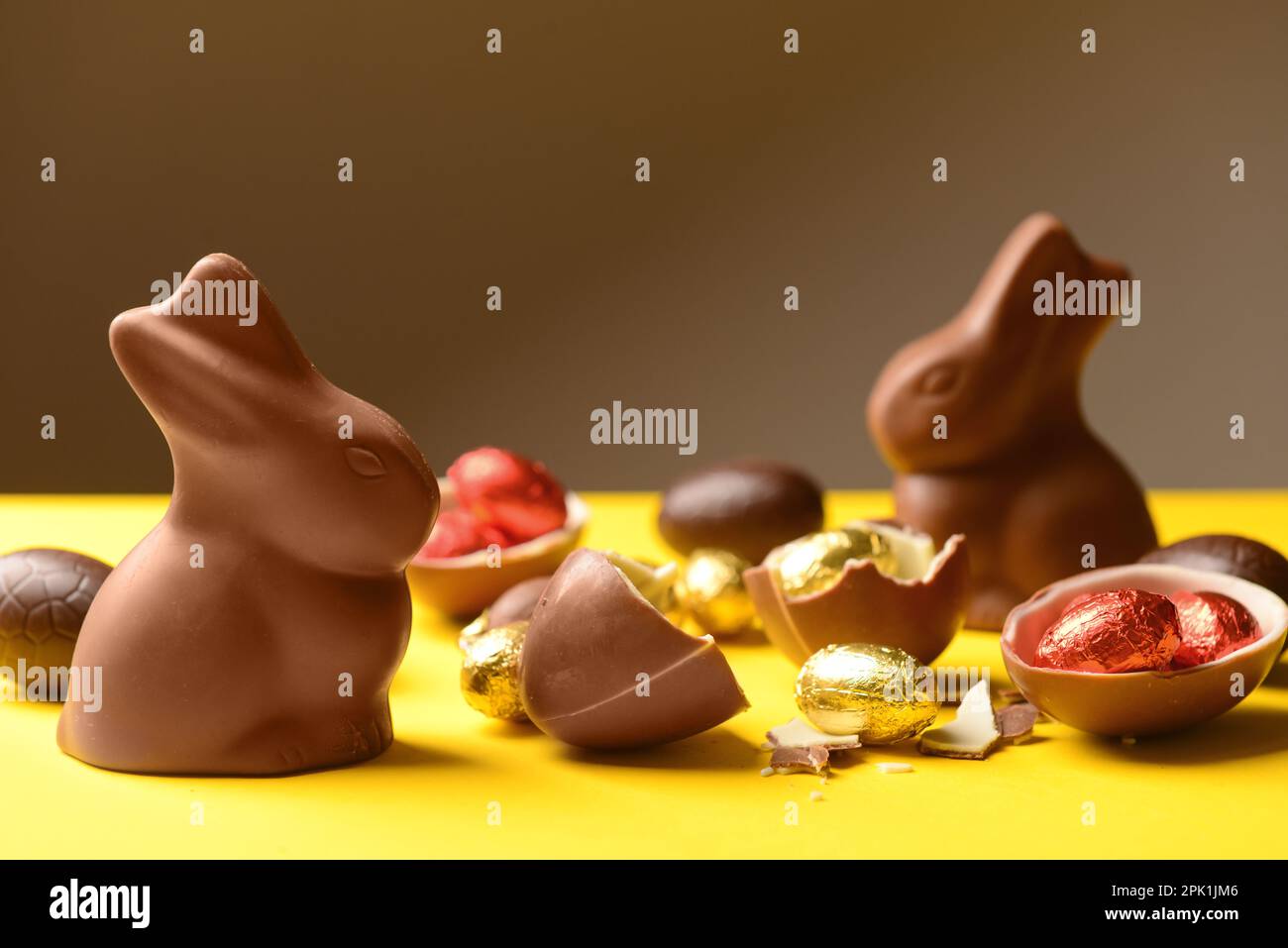 Chocolate Easter eggs and bunnies on yellow table against brown ...