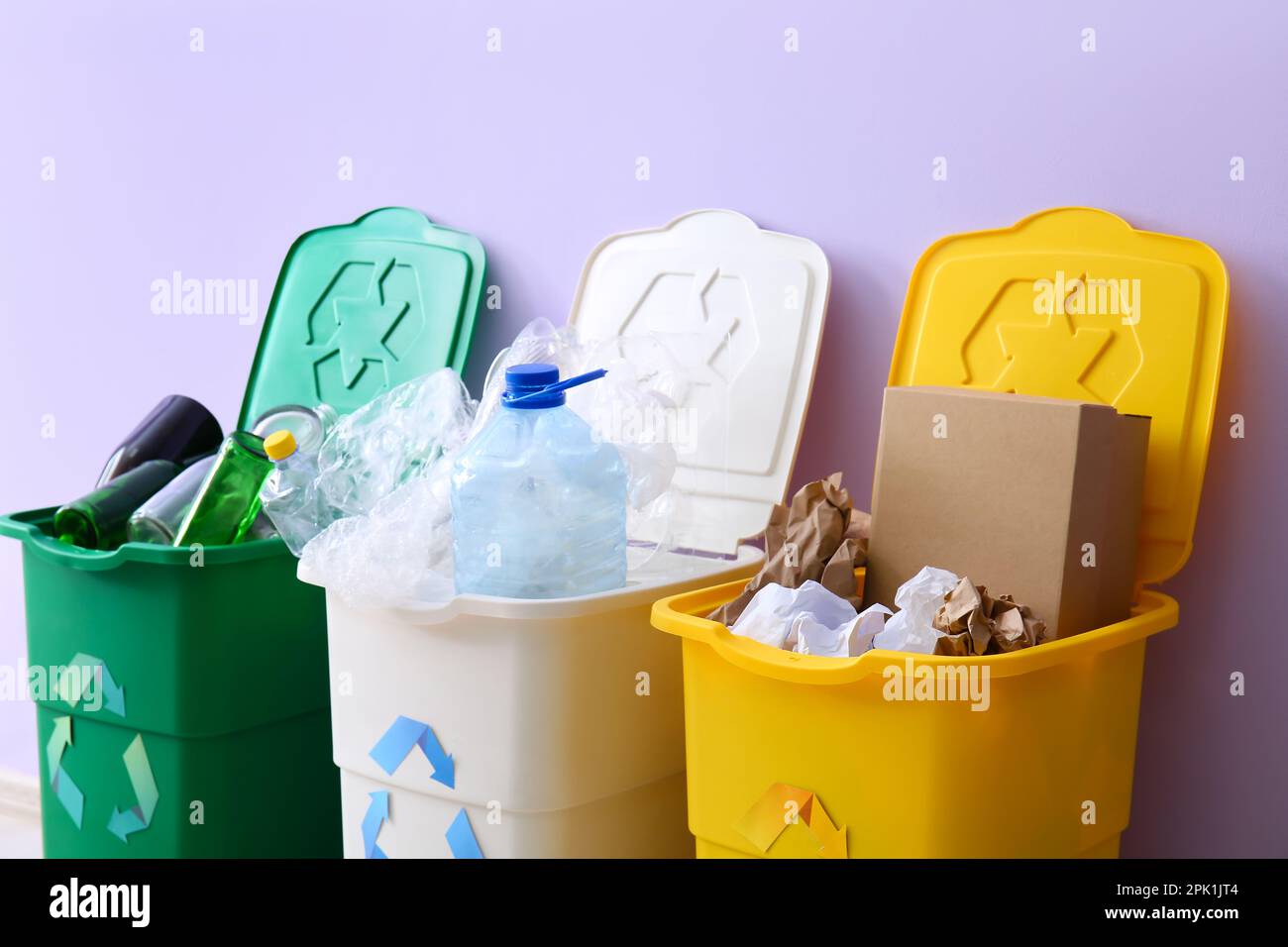 Containers with different types of garbage on lilac background ...