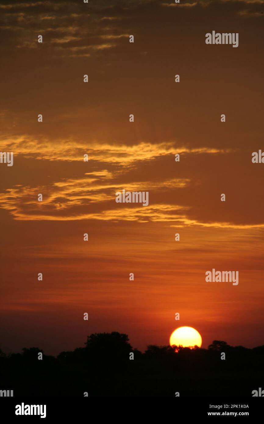 View of setting sun and sky and clouds soaked in reddish orange hue ...