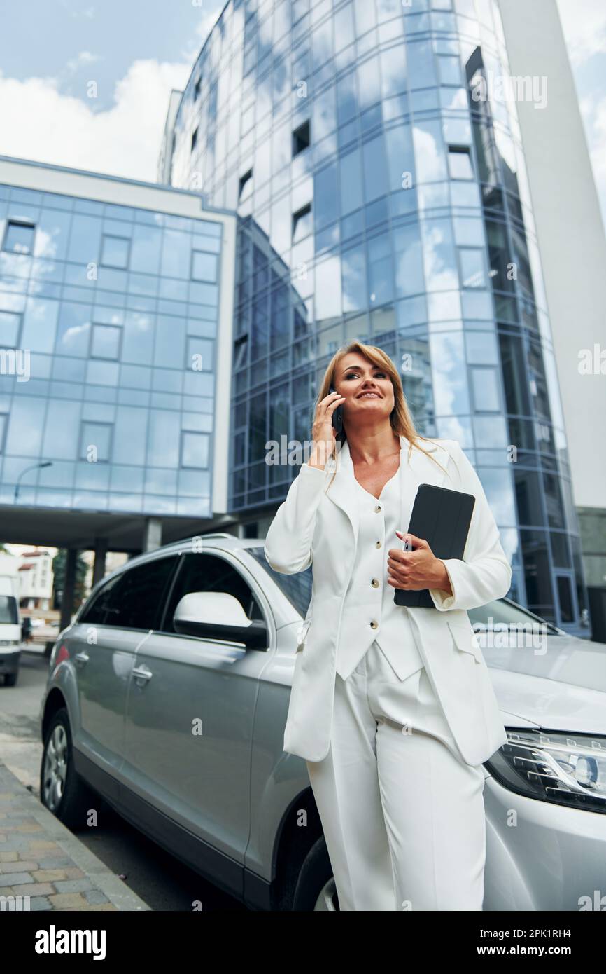 White car at background. Woman in formal wear standing outdoors in the ...