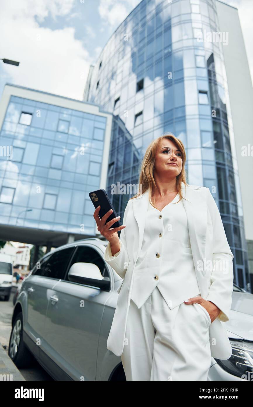 White car at background. Woman in formal wear standing outdoors in the ...