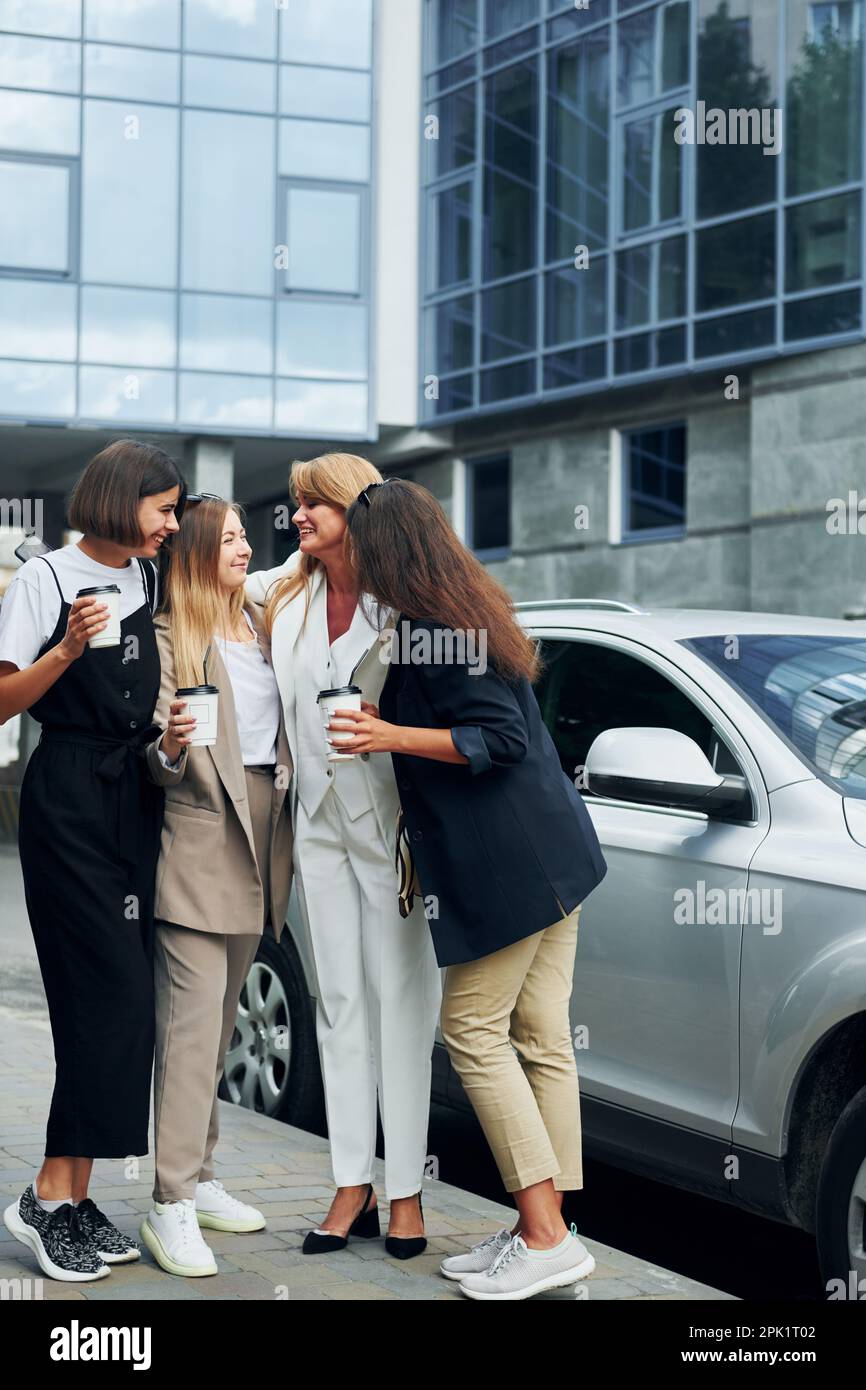 Women in formal wear is outdoors in the city together standing near ...