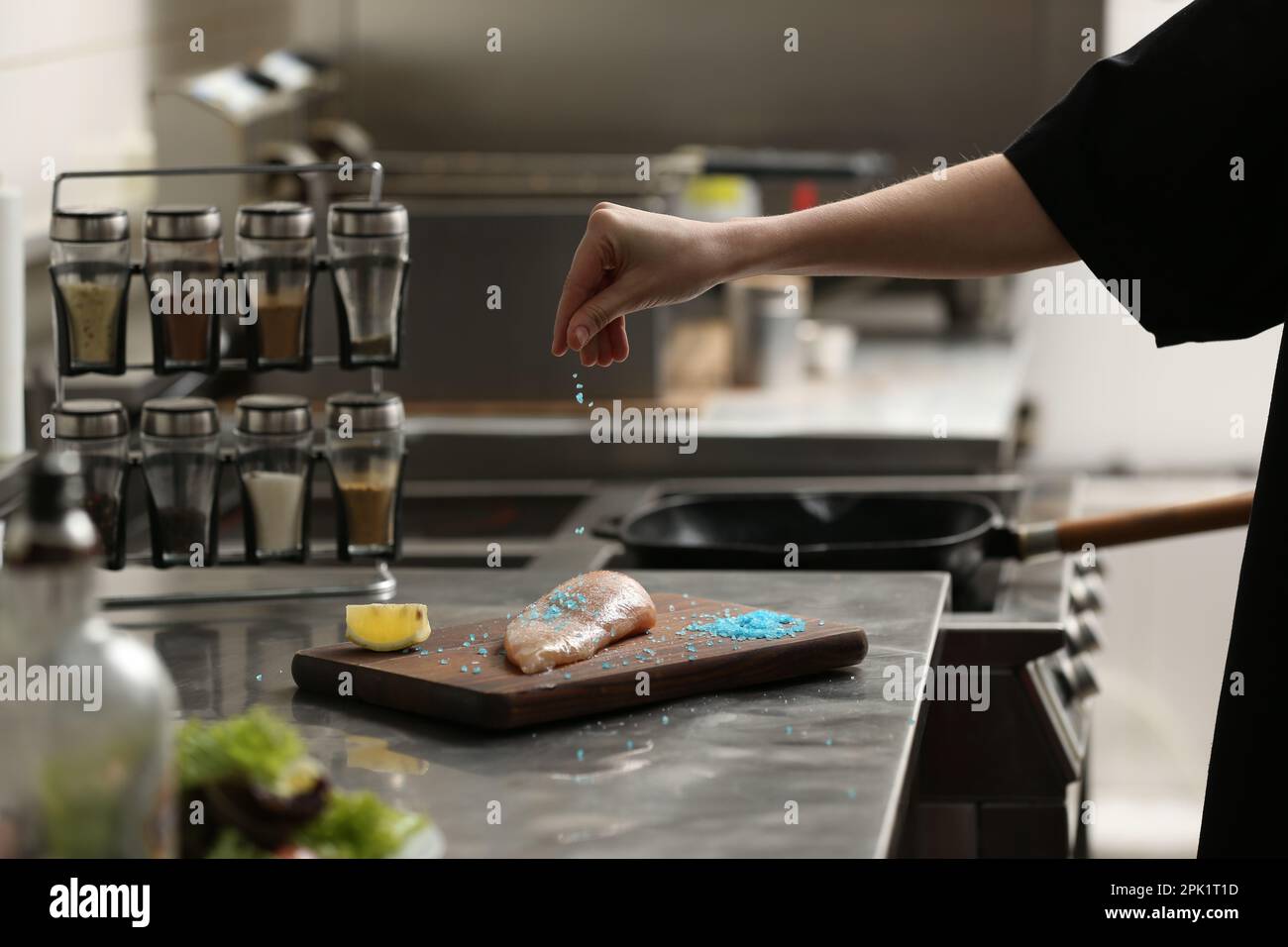 Female chef adding blue salt to raw chicken fillet in restaurant ...