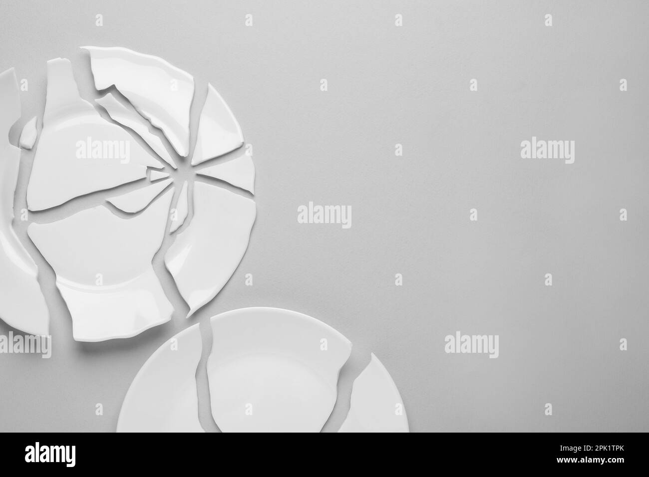 Two broken ceramic plates on light grey background, flat lay. Space for ...