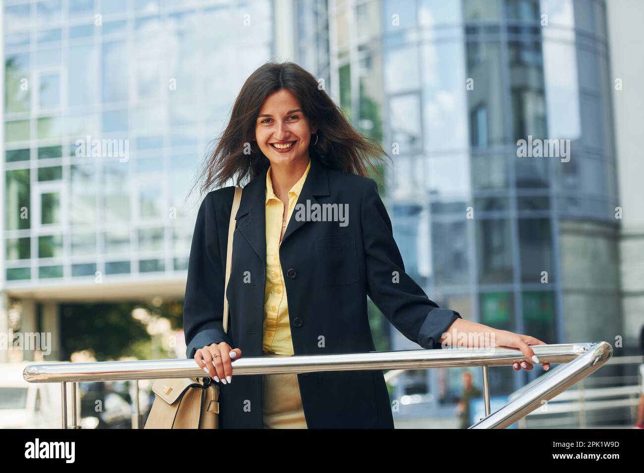 Cheerful woman in formal wear standing outdoors in the city at daytime ...