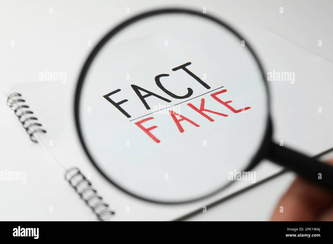 Woman holding magnifying glass over notebook with words Fact and Fake ...