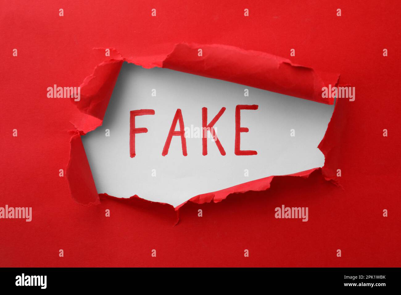 Word Fake written on white background, view through hole in red torn ...