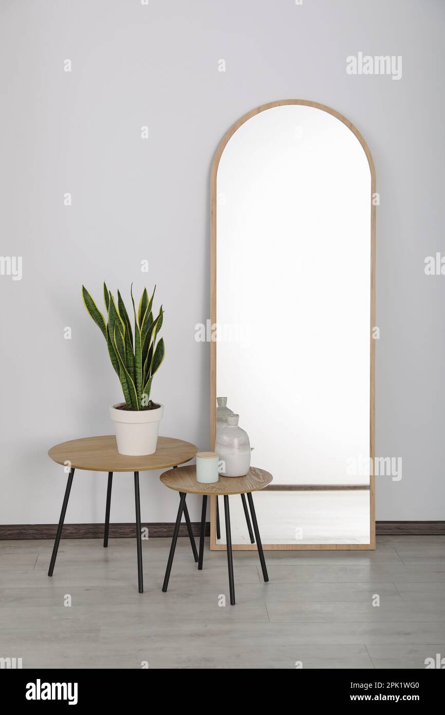 Leaning floor mirror near nesting tables with houseplant and decor in ...