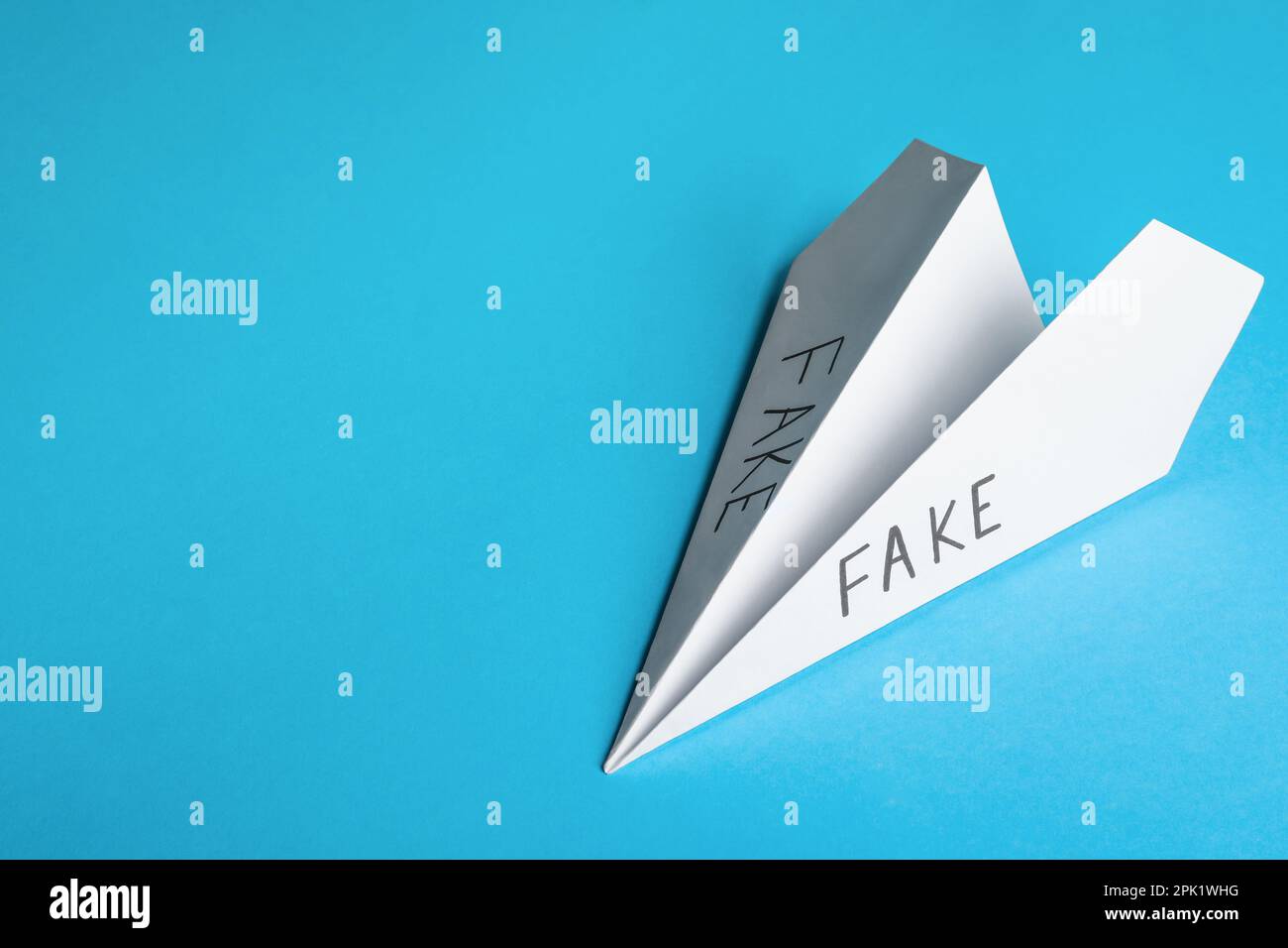 Paper plane with words FAKE on light blue background, top view. Space ...