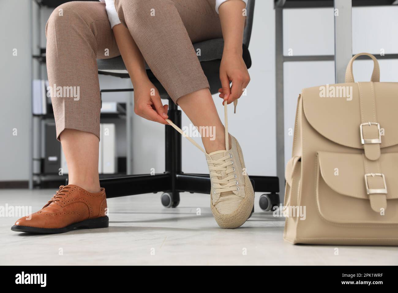 Woman taking off uncomfortable shoes and putting on sneakers in office ...