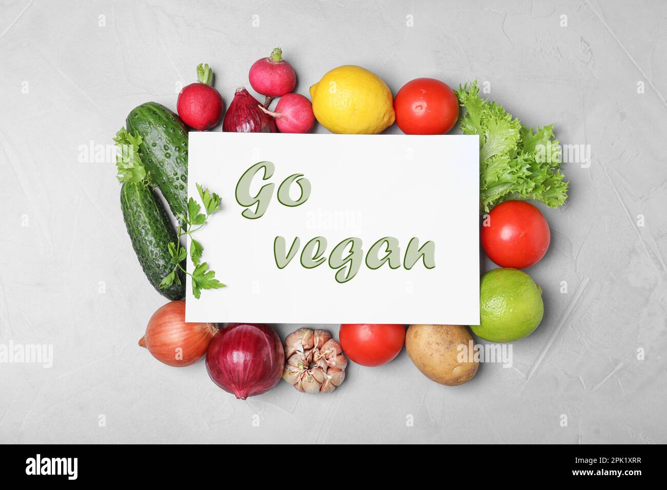 Paper card with phrase Go Vegan and fresh vegetables on light grey ...