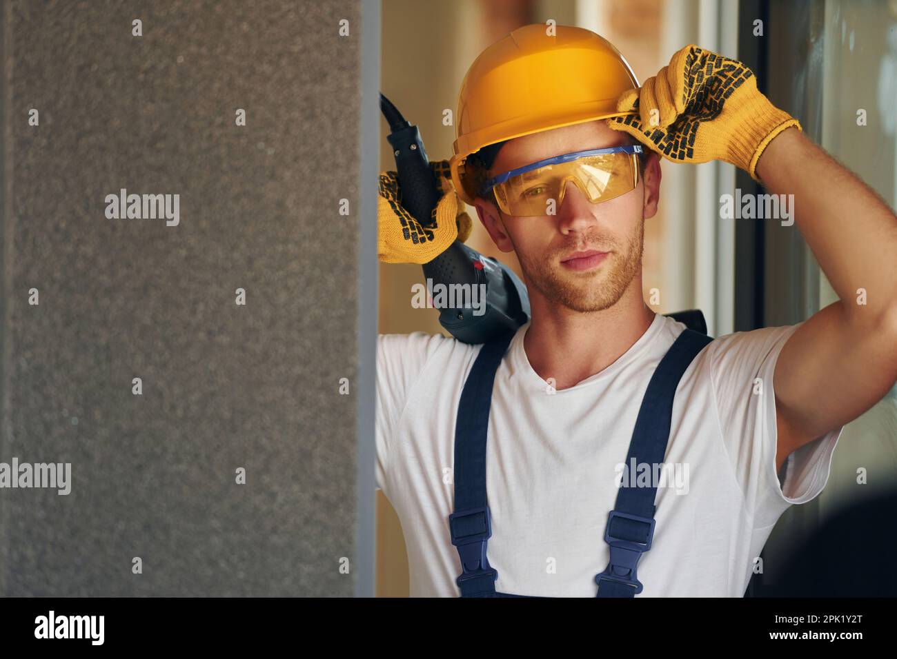 Using tool. Young man working in uniform at construction at daytime ...