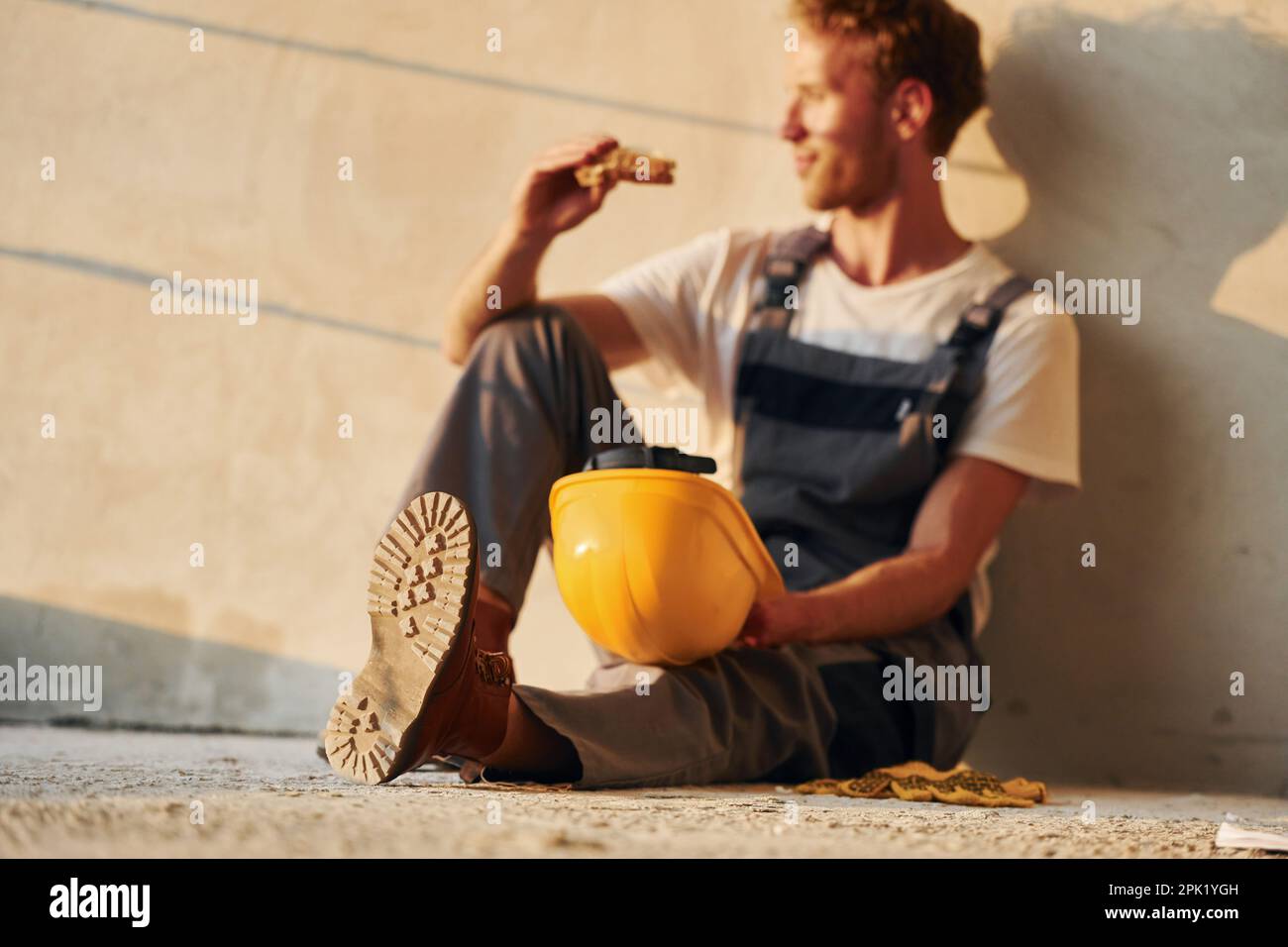 Eating food. Young man working in uniform at construction at daytime ...