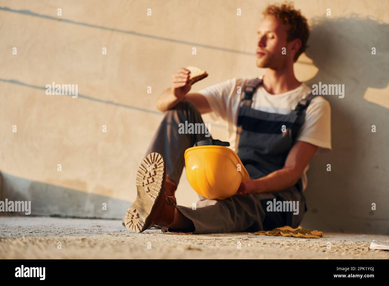 Eating food. Young man working in uniform at construction at daytime ...