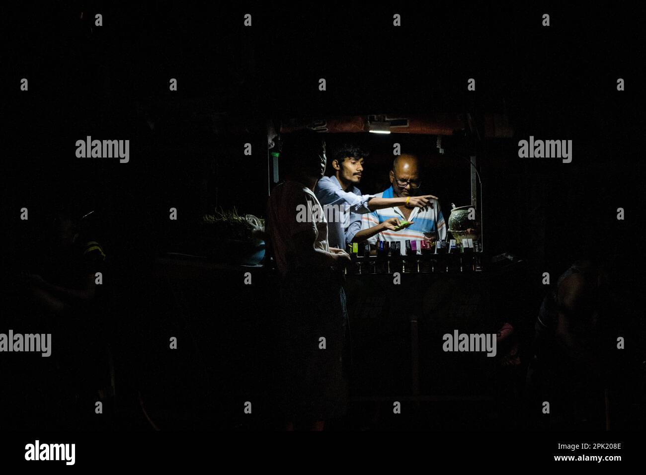 Betel nut vendors prepare their product under a tiny lamp powered by a ...