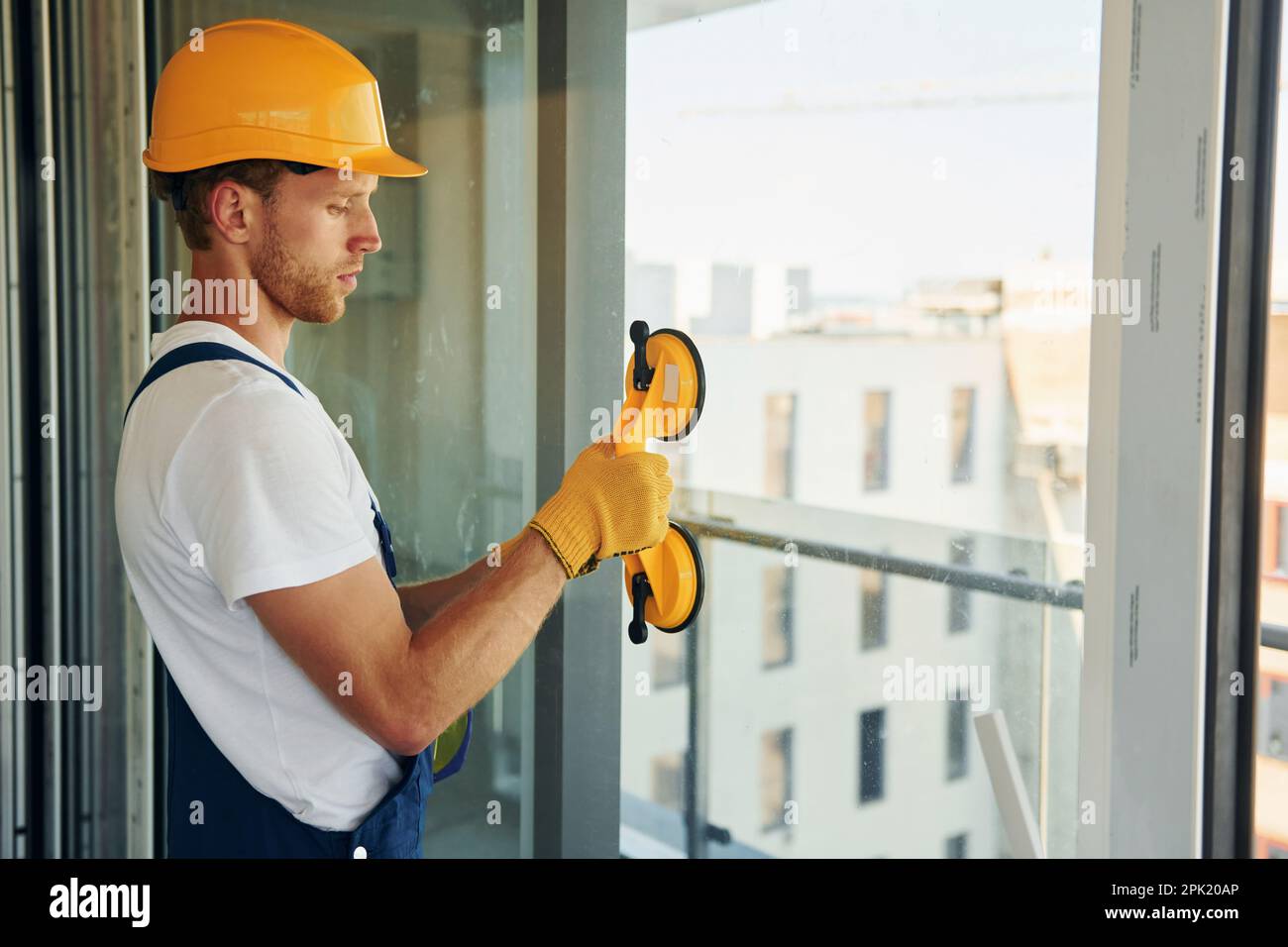 Using tool on glass. Young man working in uniform at construction at ...