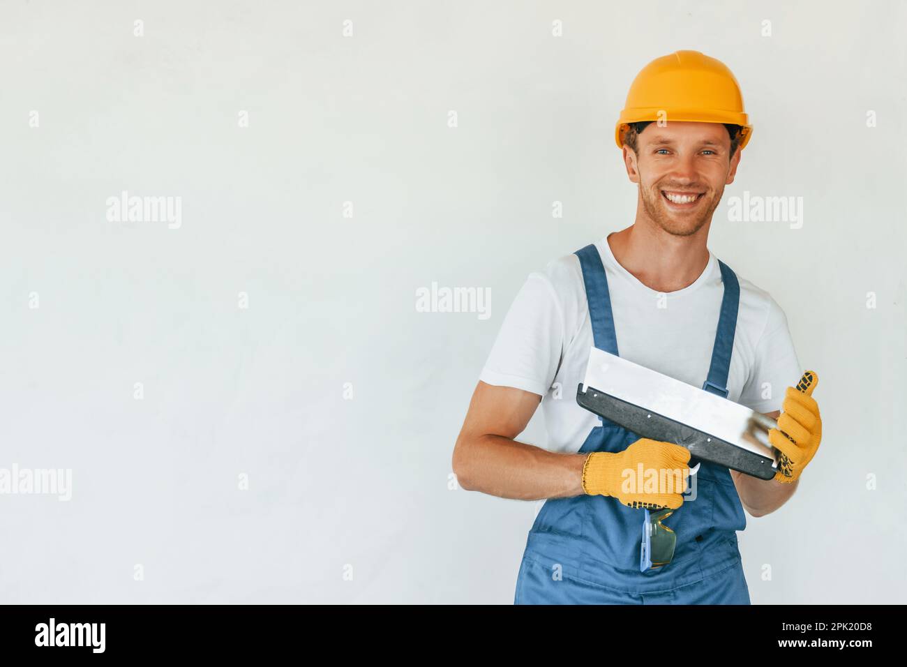 Standing near white wall. Young man working in uniform at construction ...