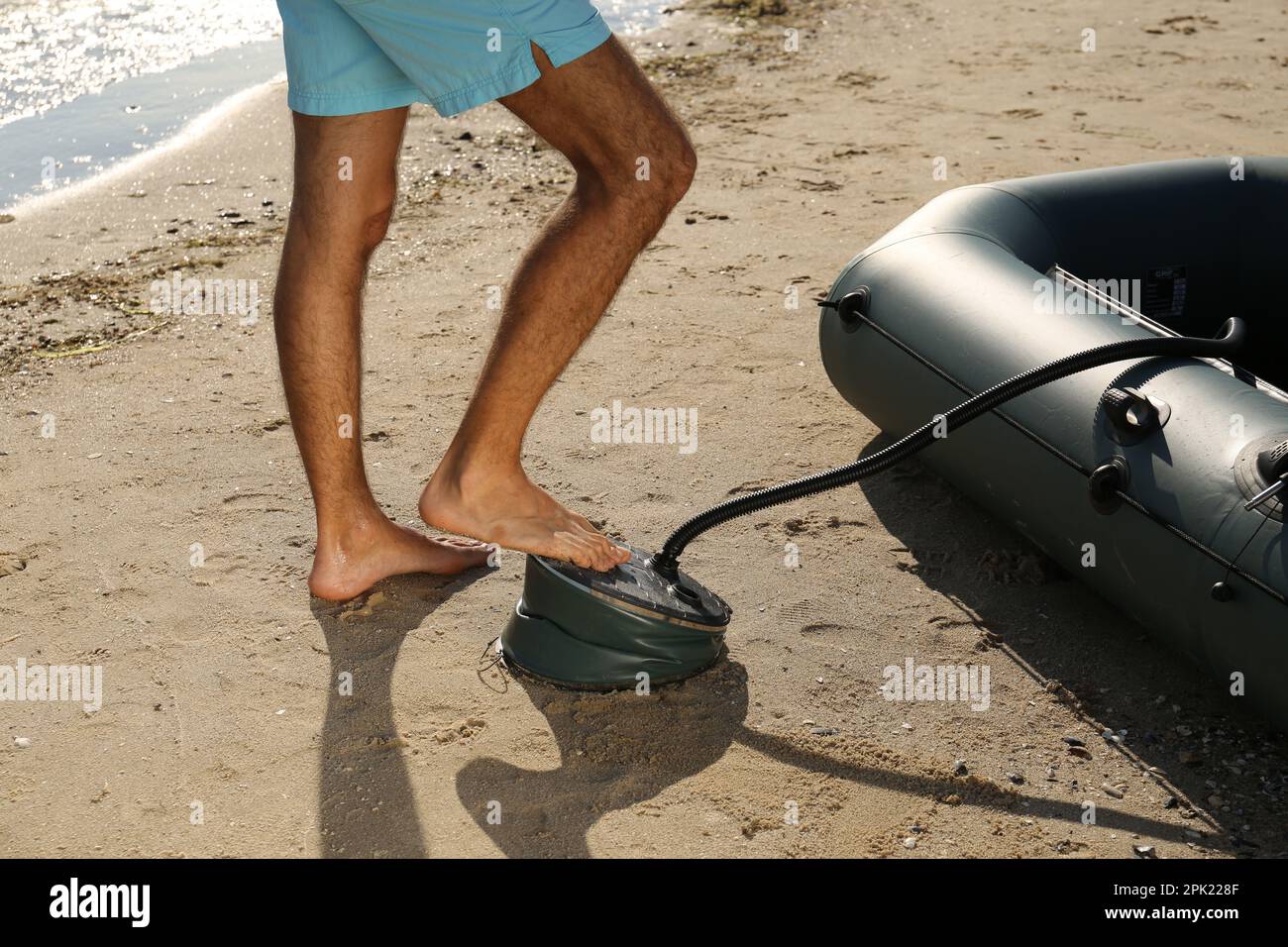 Man pumping inflatable rubber fishing boat at sandy beach on sunny day ...