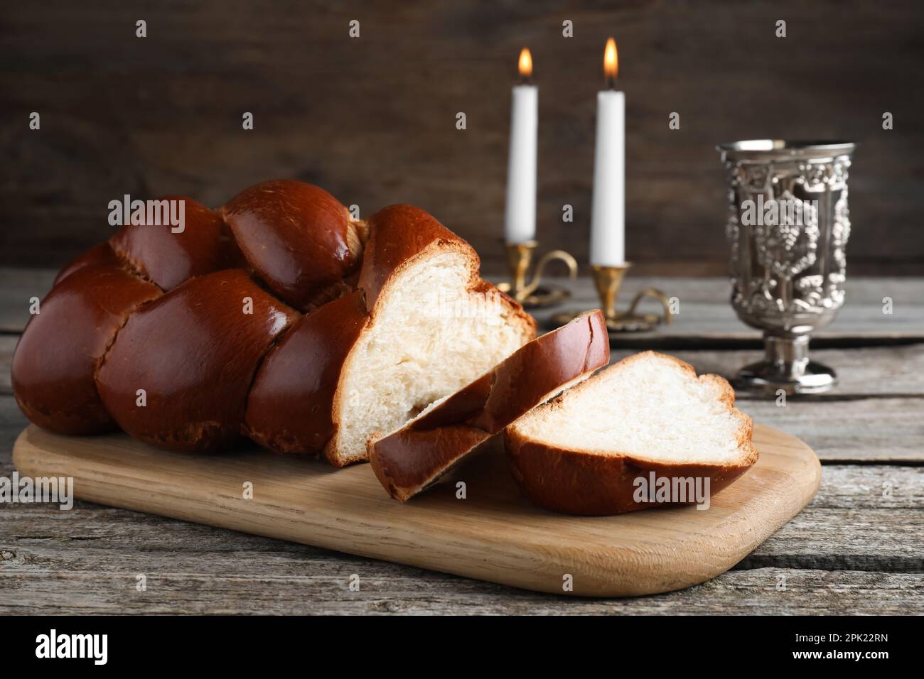 Cut homemade braided bread, goblet and candles on wooden table ...