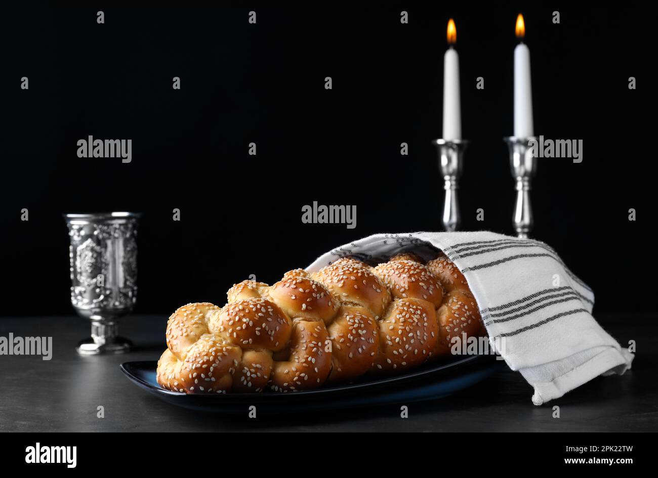Homemade braided bread with sesame seeds, goblet and candles on dark ...