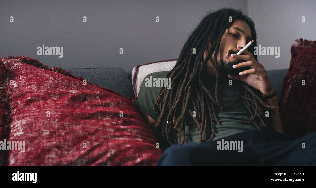 Laying back with a blunt. a young man smoking a marijuana joint at home ...