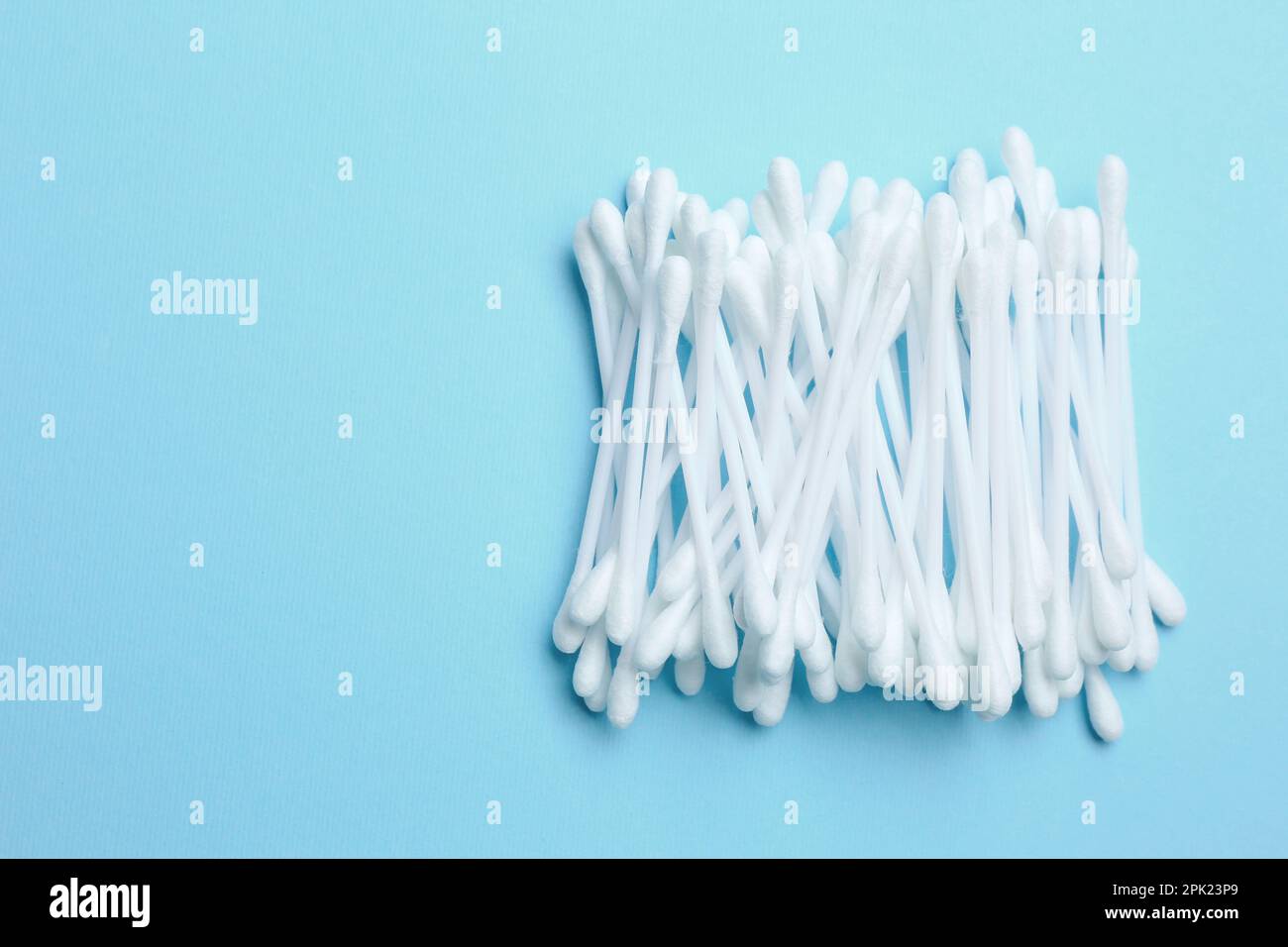 Heap of cotton buds on light blue background, top view. Space for text ...