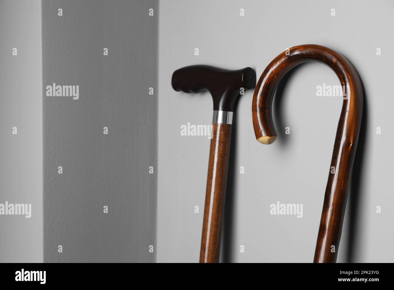 Different walking canes near light grey wall, closeup. Space for text ...