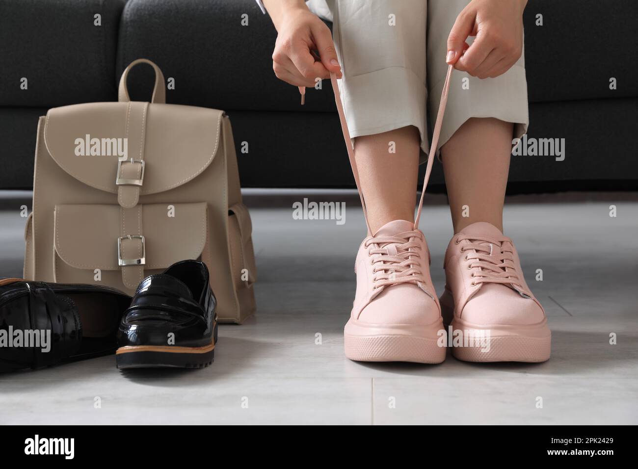 Woman taking off uncomfortable shoes and putting on sneakers in office ...