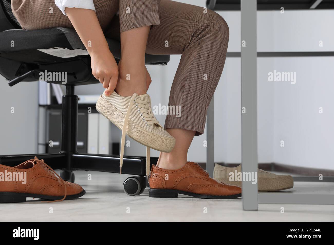 Woman taking off uncomfortable shoes and putting on sneakers in office ...