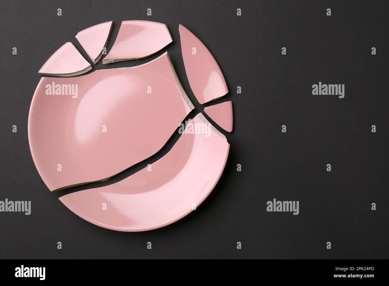 Pieces of broken pink ceramic plate on dark grey background, top view ...
