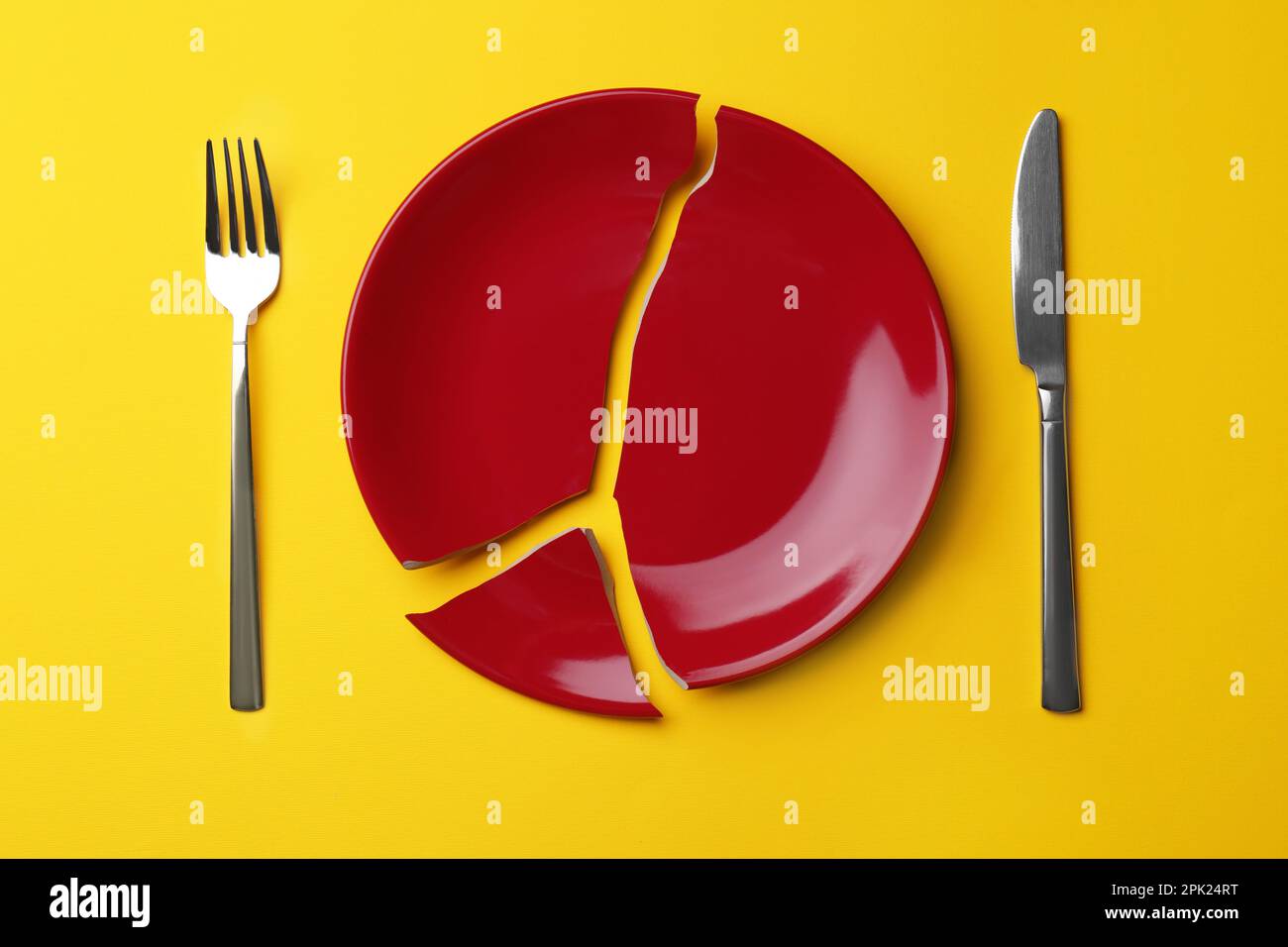 Pieces of broken red ceramic plate and cutlery on yellow background ...