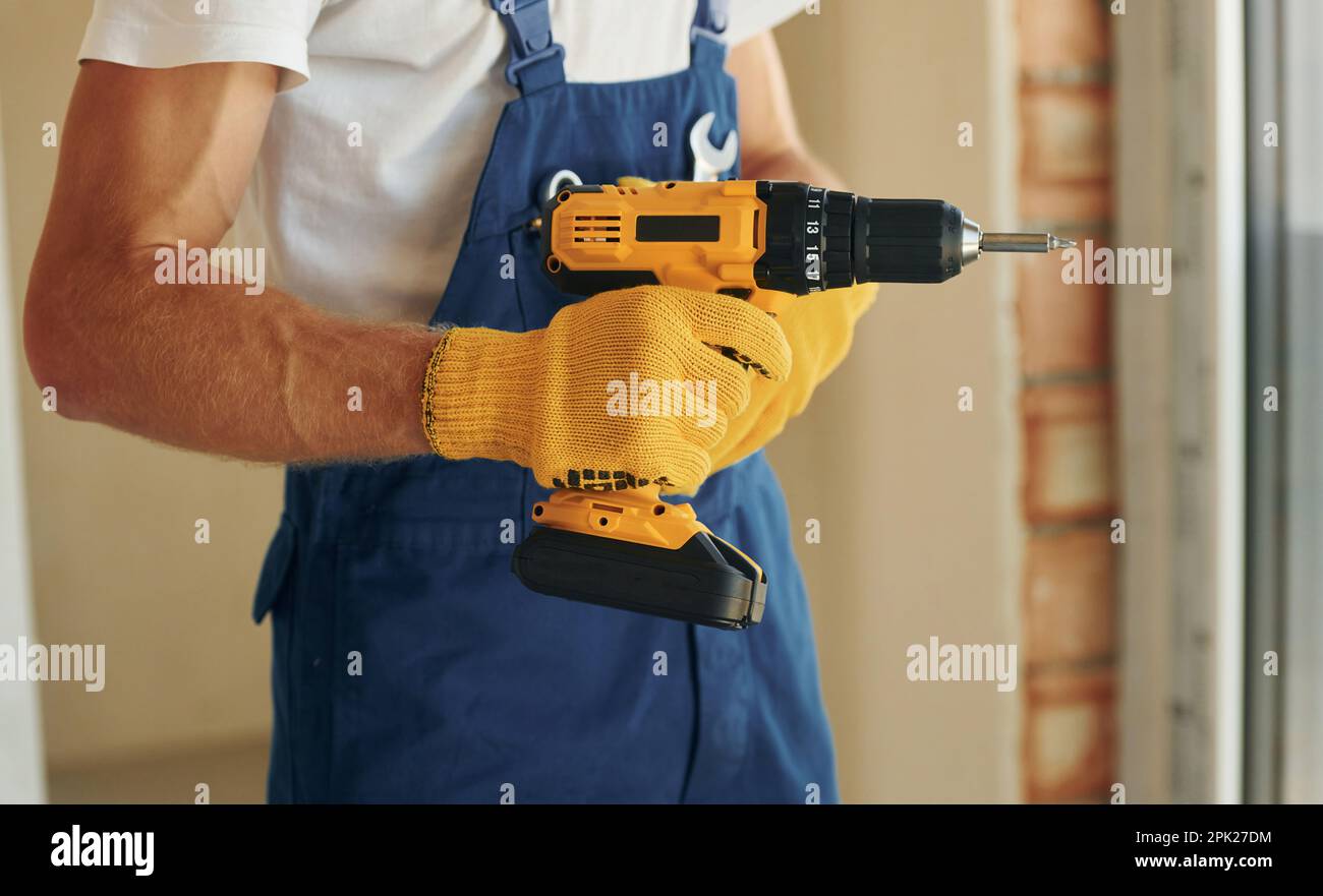 Using tool. Young man working in uniform at construction at daytime ...