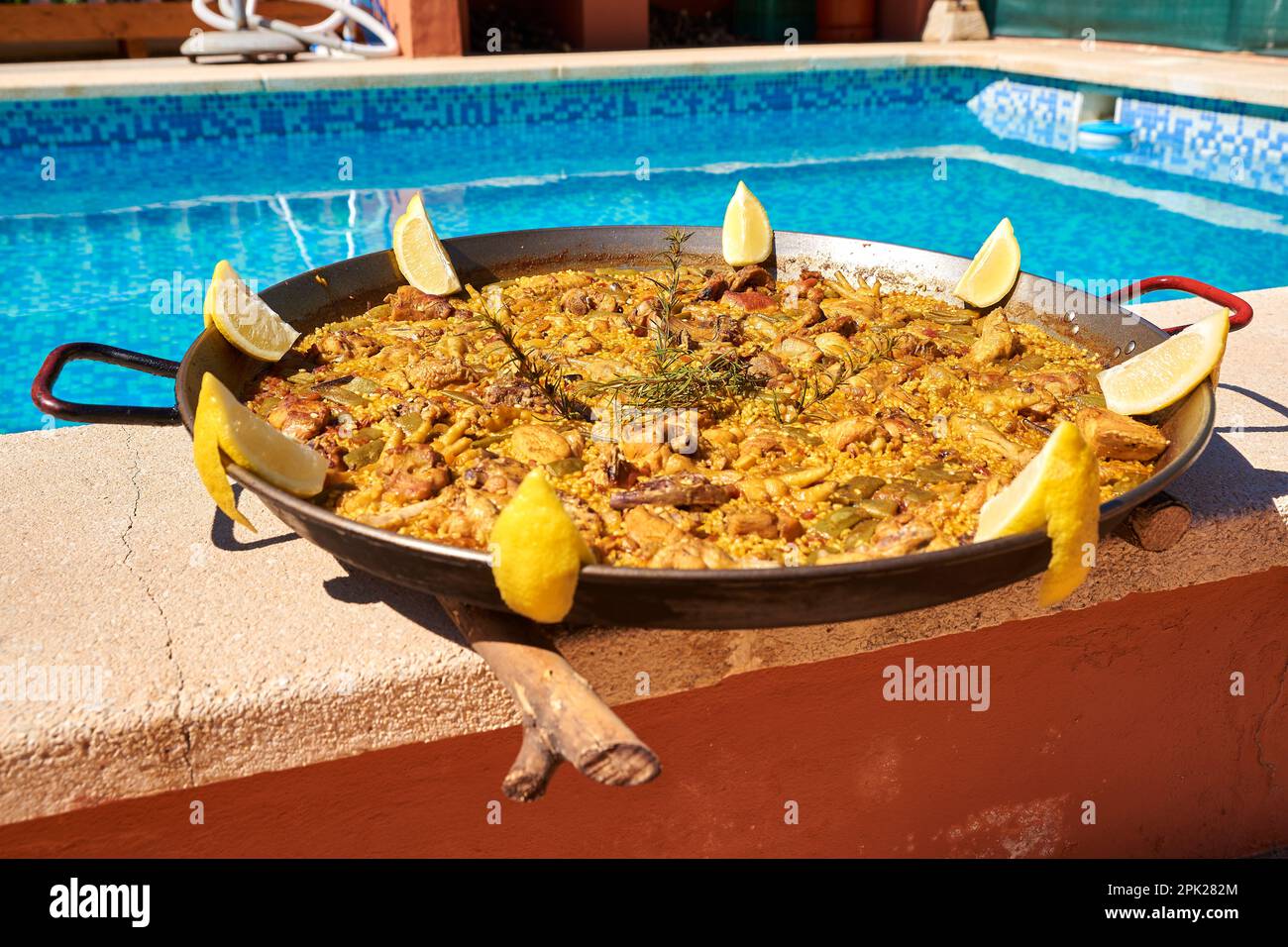 traditional paella with lemon slices decorating next to a swimming pool ...