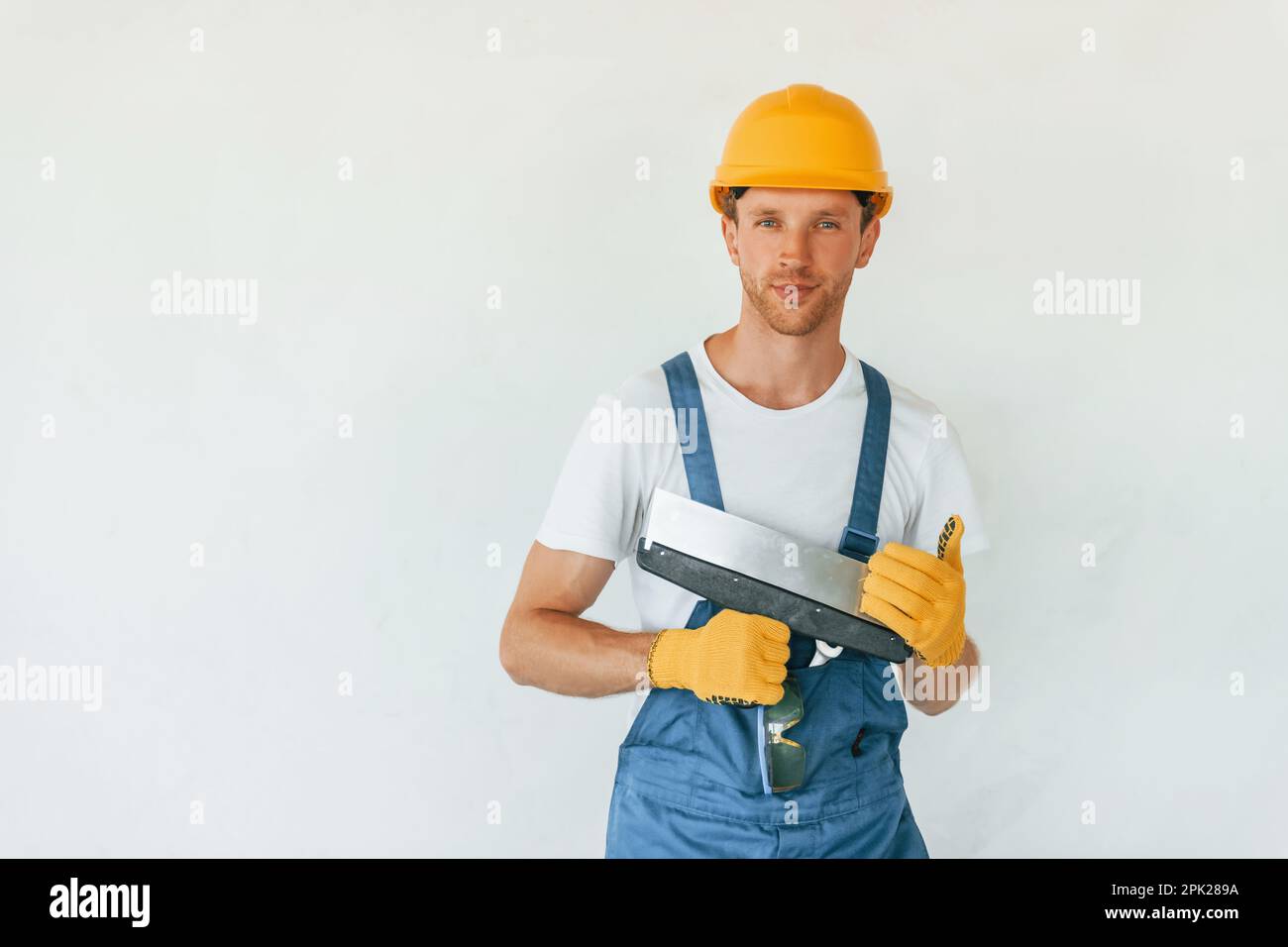Standing near white wall. Young man working in uniform at construction ...
