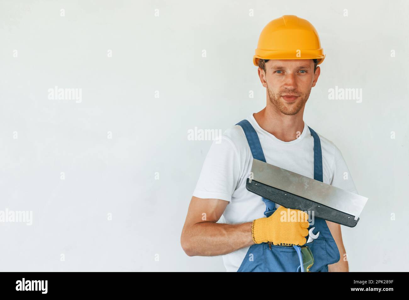 Standing near white wall. Young man working in uniform at construction ...