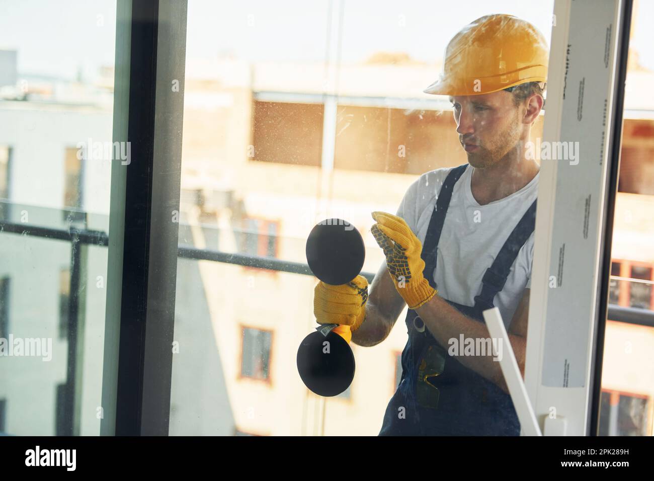 Using tool on glass. Young man working in uniform at construction at ...