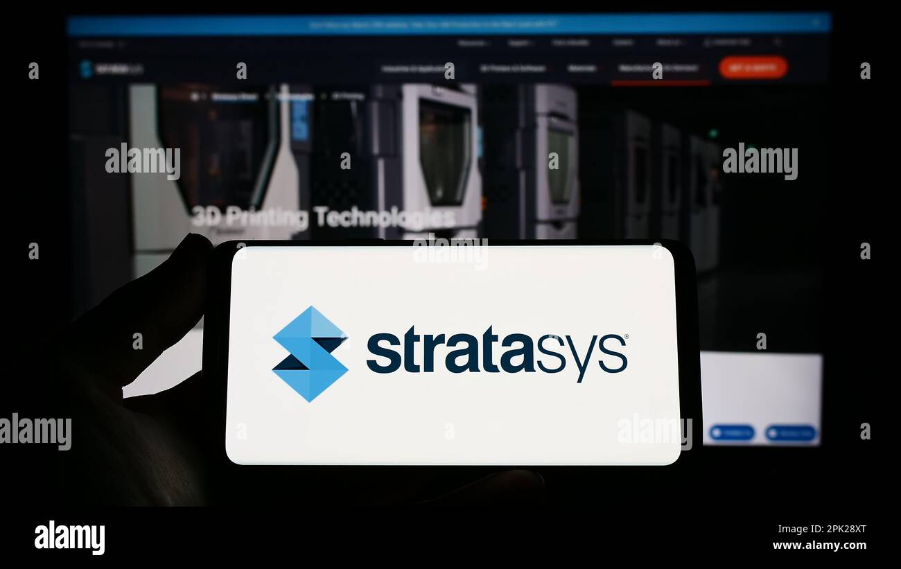 Person holding smartphone with logo of 3D printing company Stratasys Ltd. on screen in front of ...