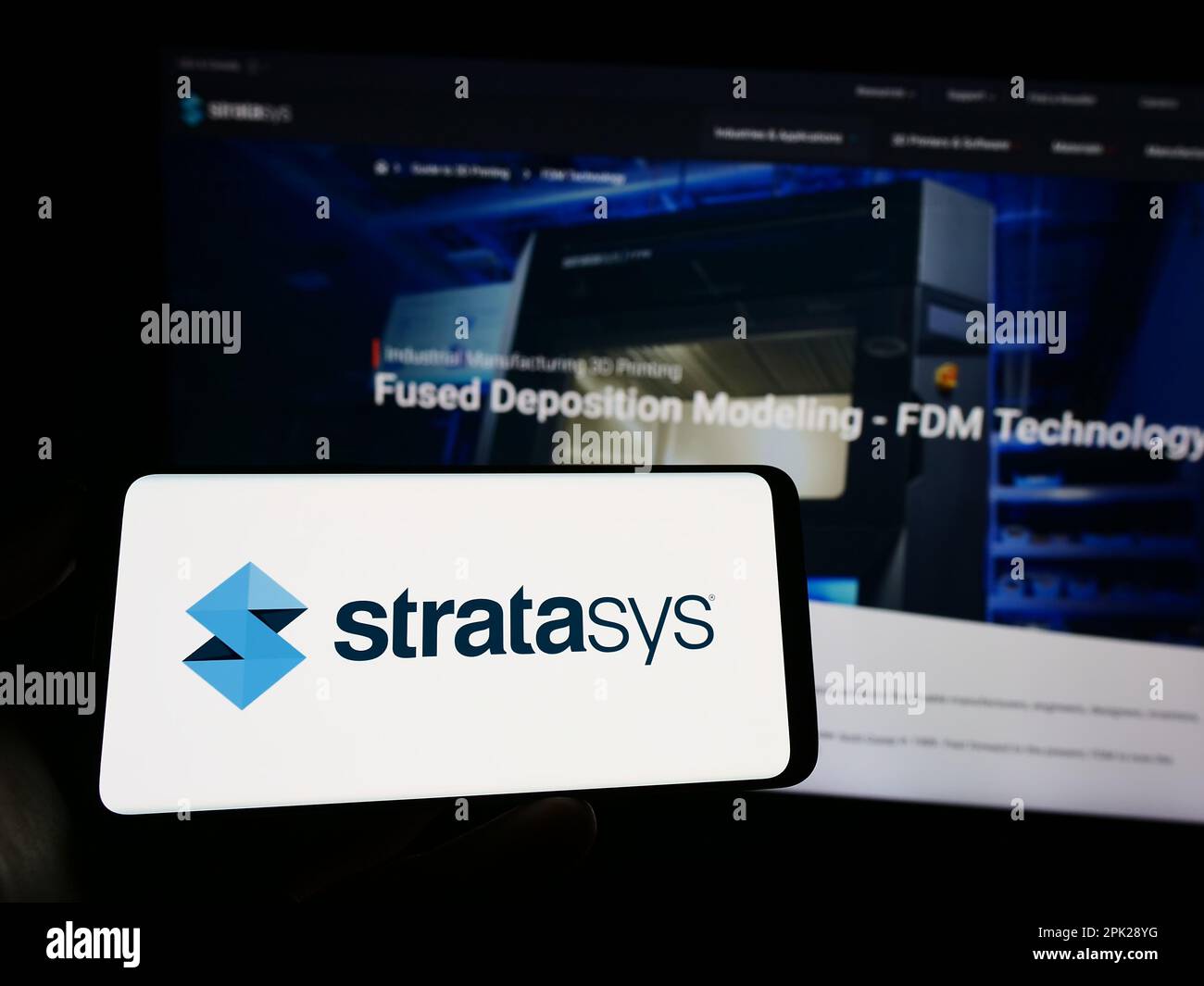 Person holding cellphone with logo of 3D printing company Stratasys Ltd ...