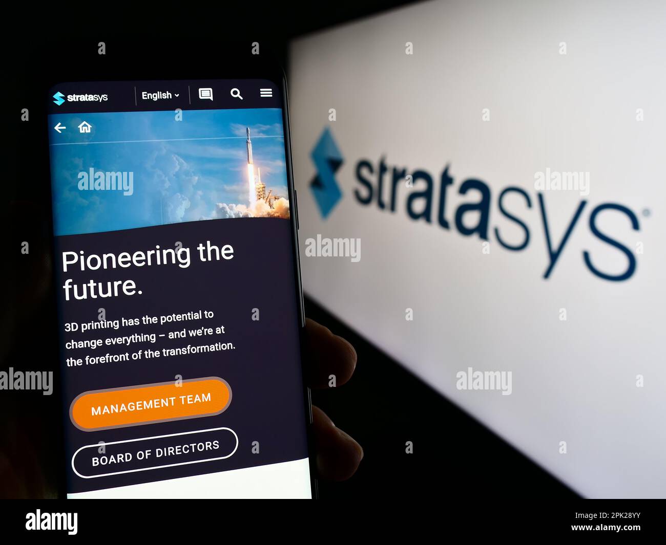 Person holding cellphone with website of 3D printing company Stratasys Ltd. on screen in front ...