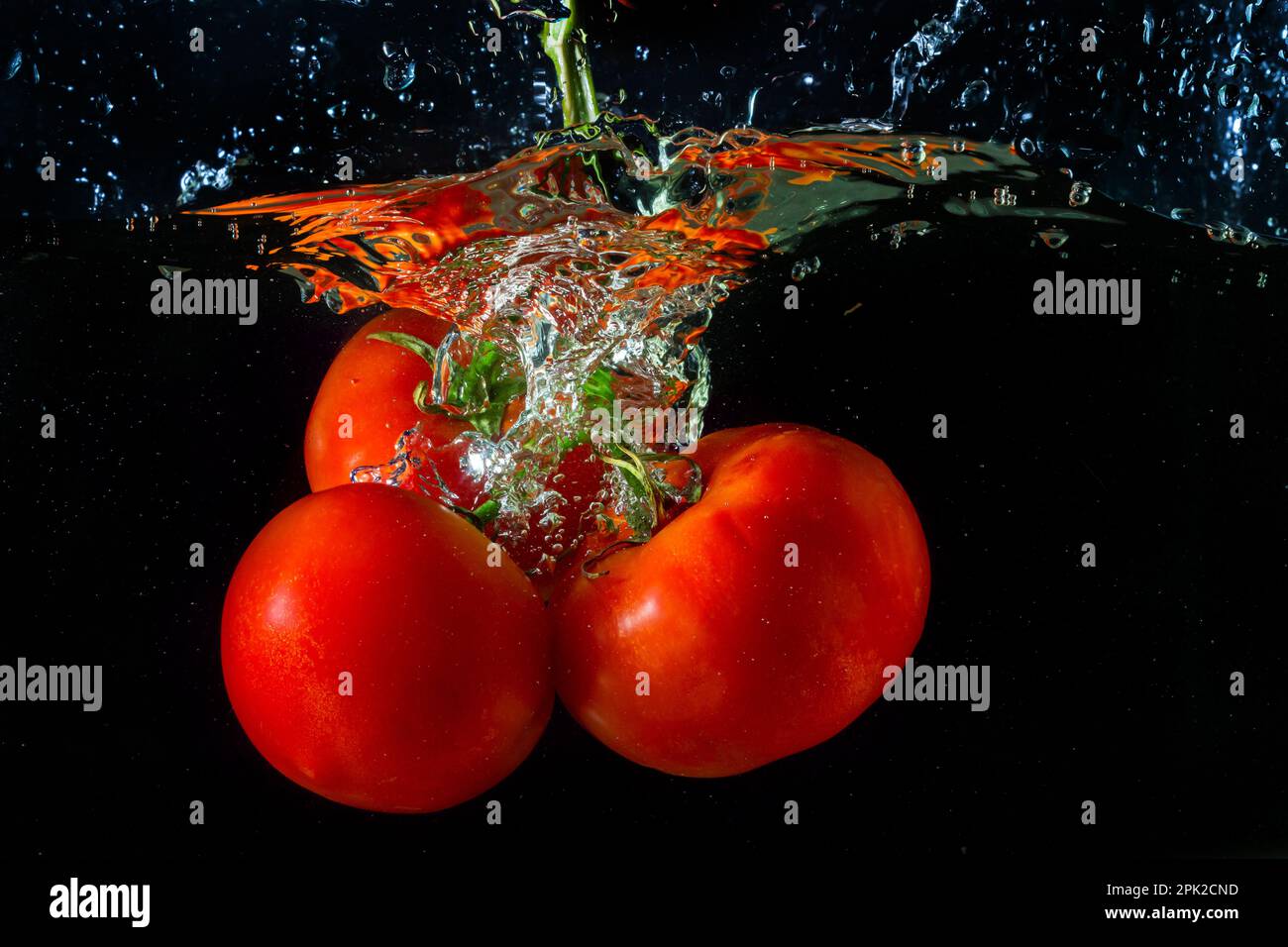 Fresh red tomato falling into water with water splash and air bubbles ...