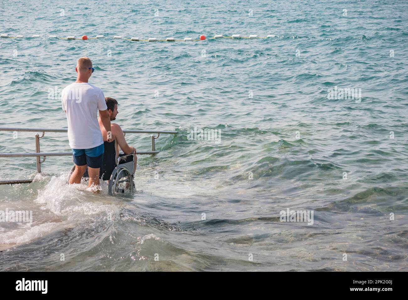 Man with disability on wheelchair at accessible beach goes swimming ...