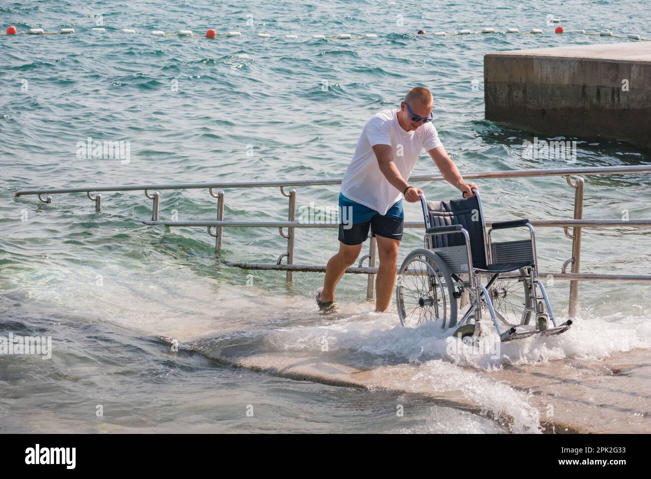 Lifeguard pushing wheelchair at sea on accessible beach with ramp for ...