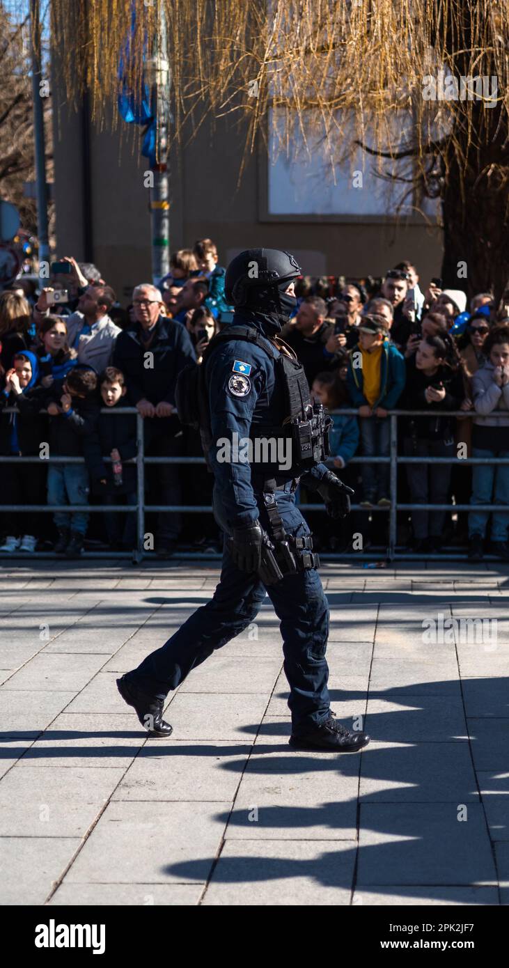 Two uniformed police officers march in front of a large crowd of people ...