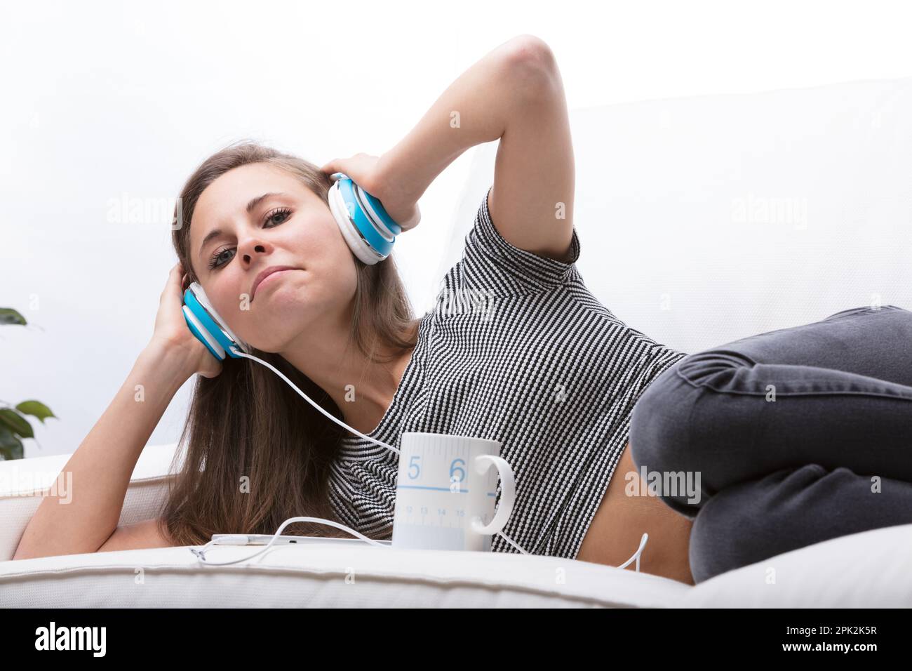 Girl lying on her side on the couch, legs curled up, listens to music ...