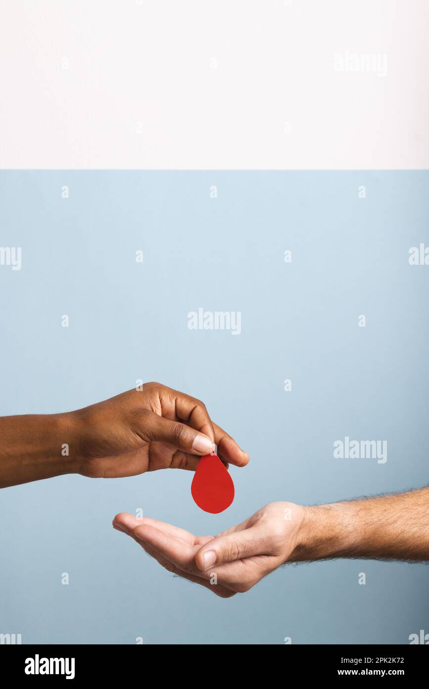 Hands of biracial man giving blood drop to caucasian man, on blue and ...