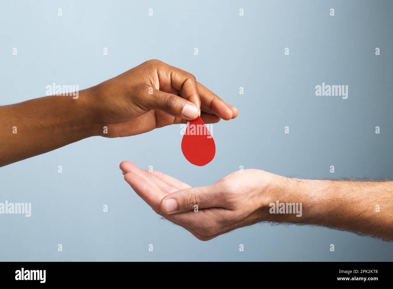 Hands of biracial man giving blood drop to caucasian man, on blue ...
