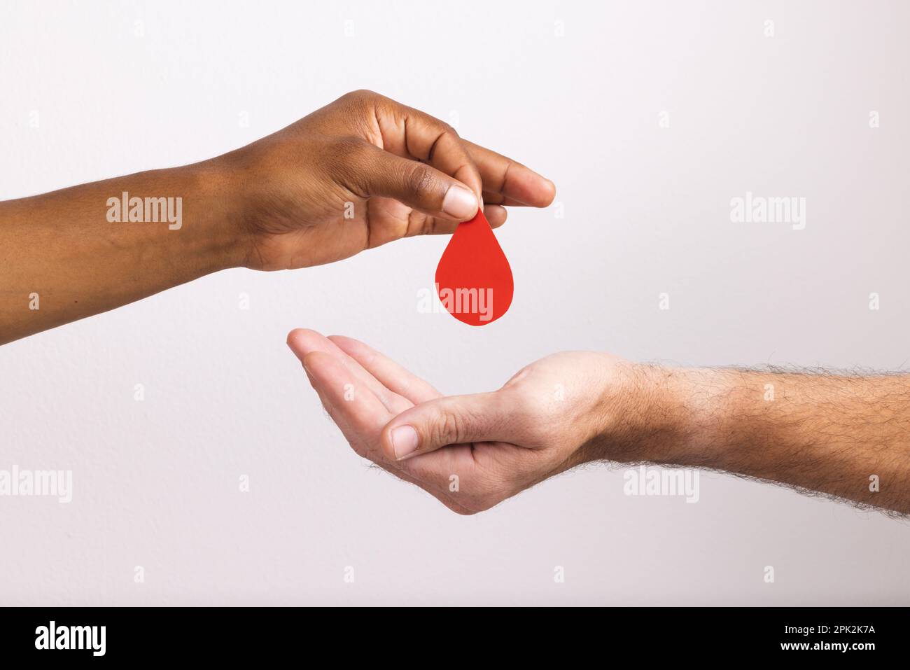 Hands of biracial man giving blood drop to caucasian man, on white ...