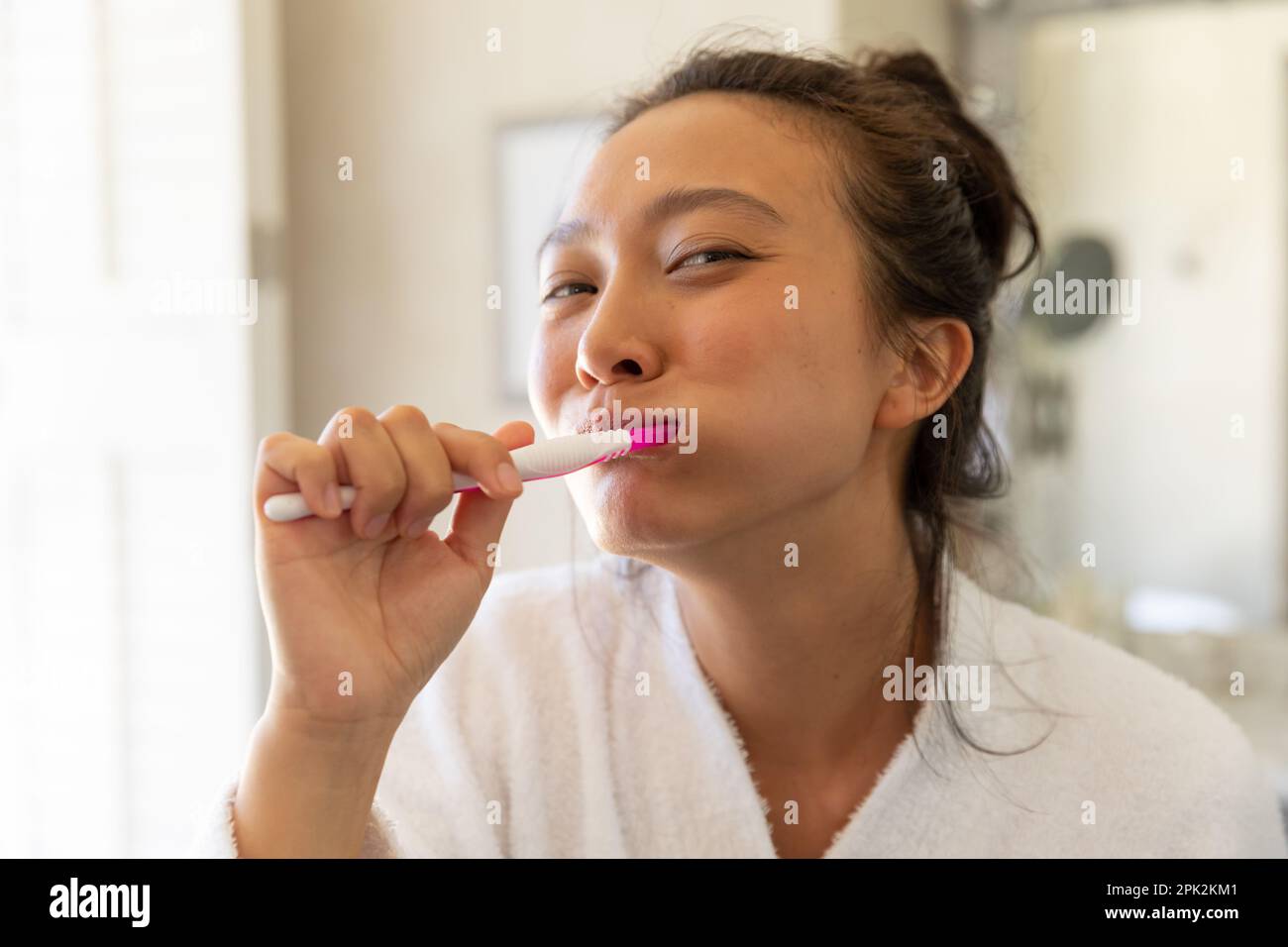 Happy Asian Woman Wearing Bathrobe Looking In Bathroom Mirror Brushing